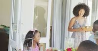 A joyful biracial mother serves bread to her multi-generational family ...
